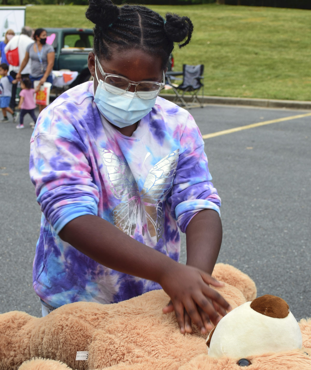 A young girl practices CPR on a large teddy bear, using instruc – Greenbelt News Review